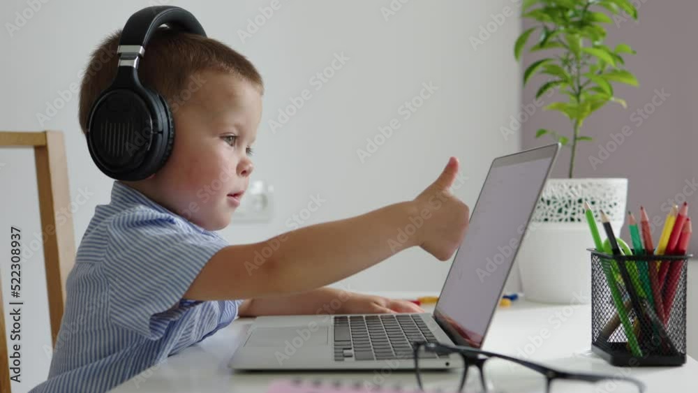 baby child boy in headphones showing thumb up to laptop computer screen ...