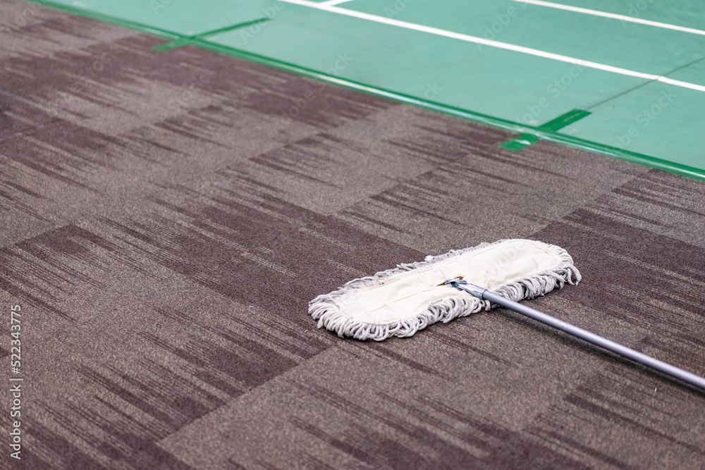 A white badminton court mop is placed in front of a black chair located ...
