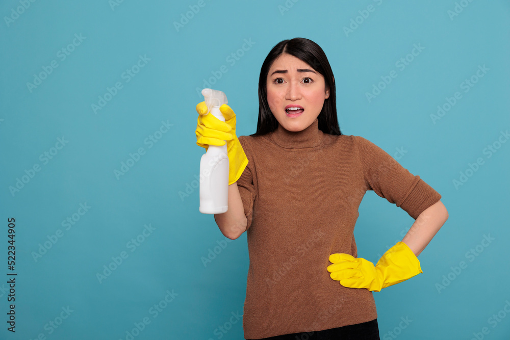 Shocked surprised asian housekeeper from chores holding spray in yellow ...