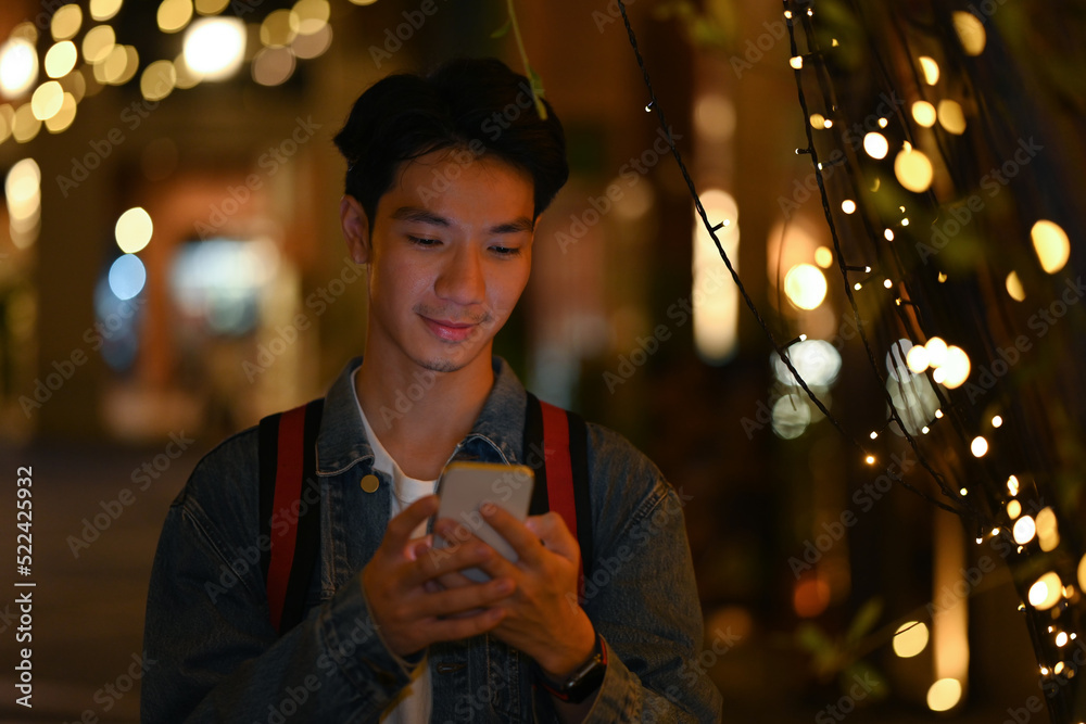 Smiling young asian male typing text message on smart phone while ...