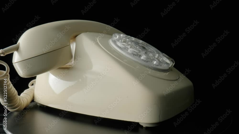 Old white rotary telephone with twisted cord rotating on black ...