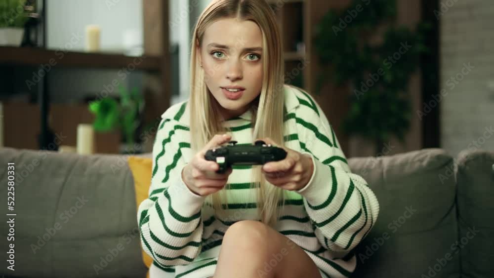Beautiful excited young gamer girl sitting on a couch and playing in ...