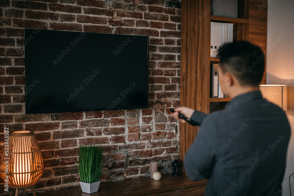 Adult chinese man with remote control turns on tv with blank screen in ...