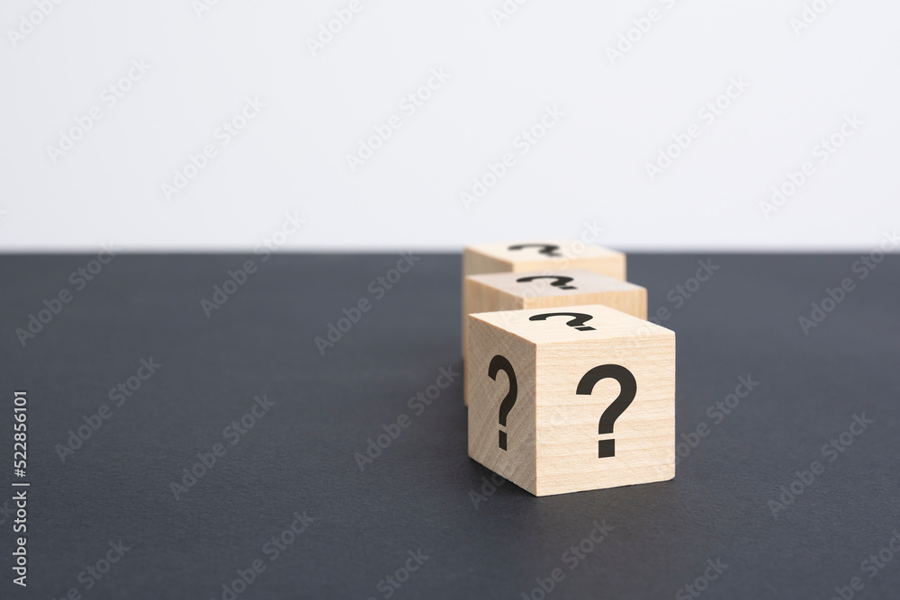 staggered row of three wooden blocks with question marks black on black ...