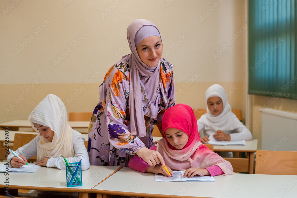 Female hijab Muslim teacher helps school children to finish the lesson ...