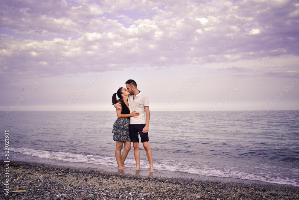 Pareja besandose en la orilla de la playa frente al mar, con un cielo ...