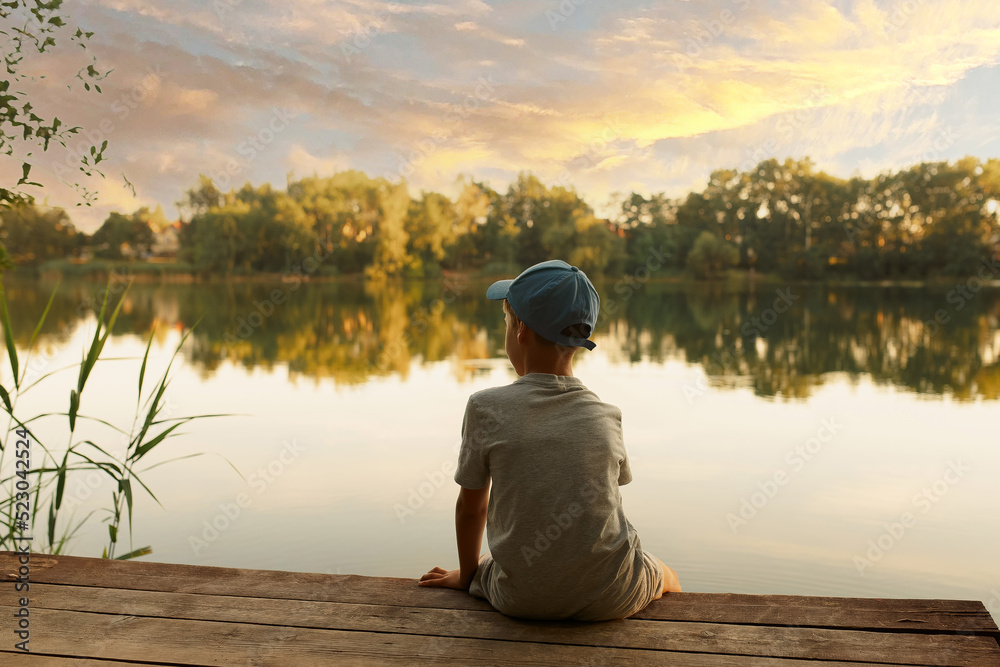 Boy on a pier by the lake. the child looks at the lake, sunset, nature ...