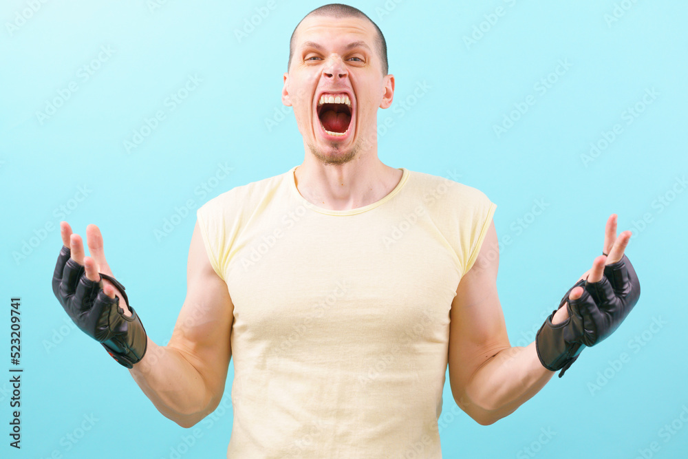 A man in black MMA gloves screams and spreads his hands on a blue ...