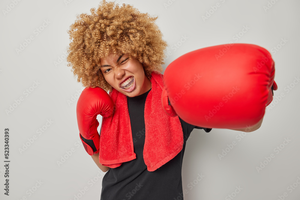 Sportive curly haired woman wears boxing gloves black t shirt and red ...