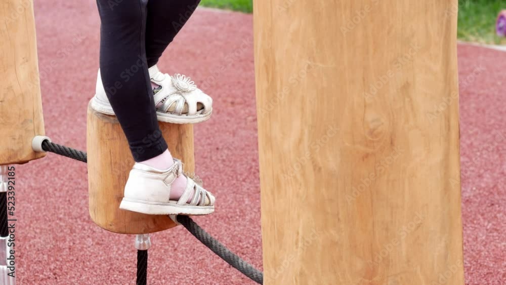 Close-up of a little girl's feet on an obstacle course rope ladder with ...