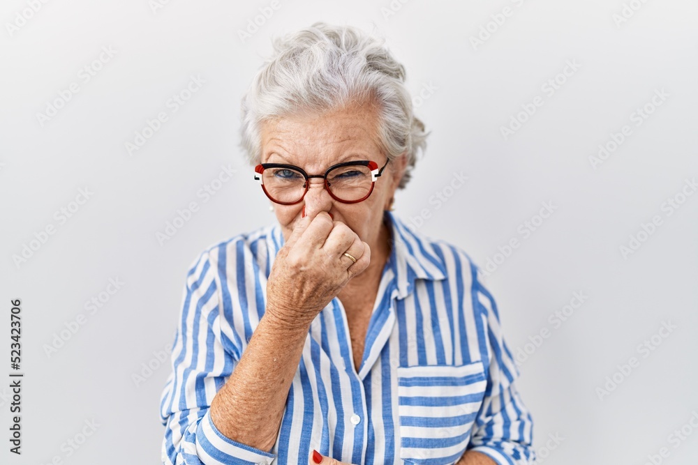Senior woman with grey hair standing over white background smelling ...