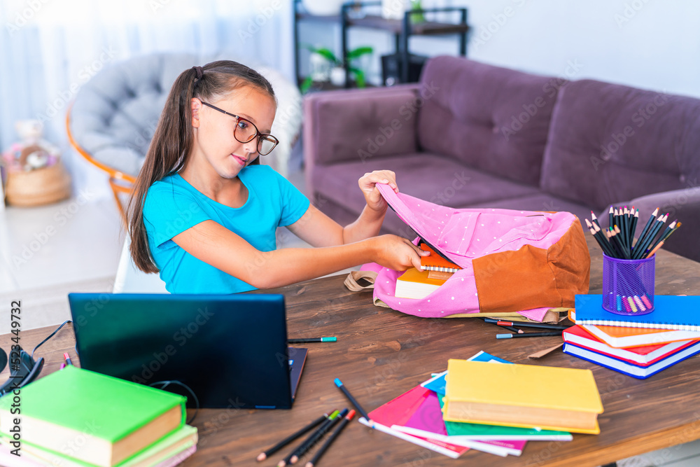 Cute happy schoolgirl puts stationery in a backpack. Preparation for ...