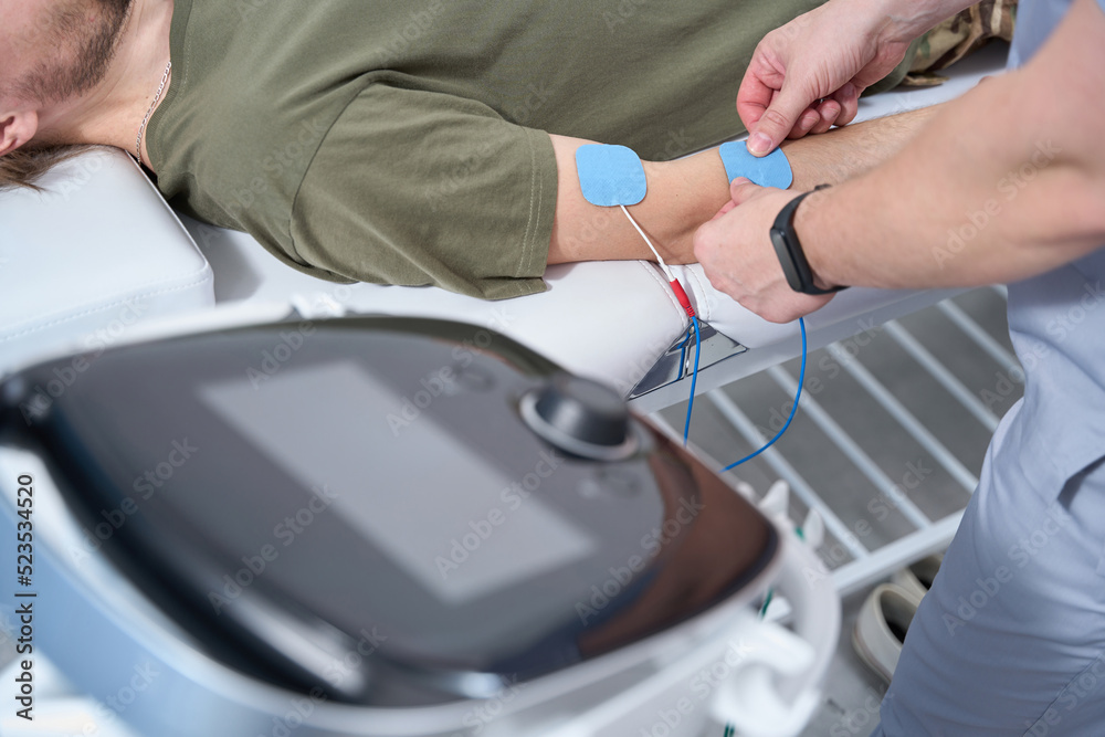 Doctor attaches electrodes to the patient hand in military sanatorium ...