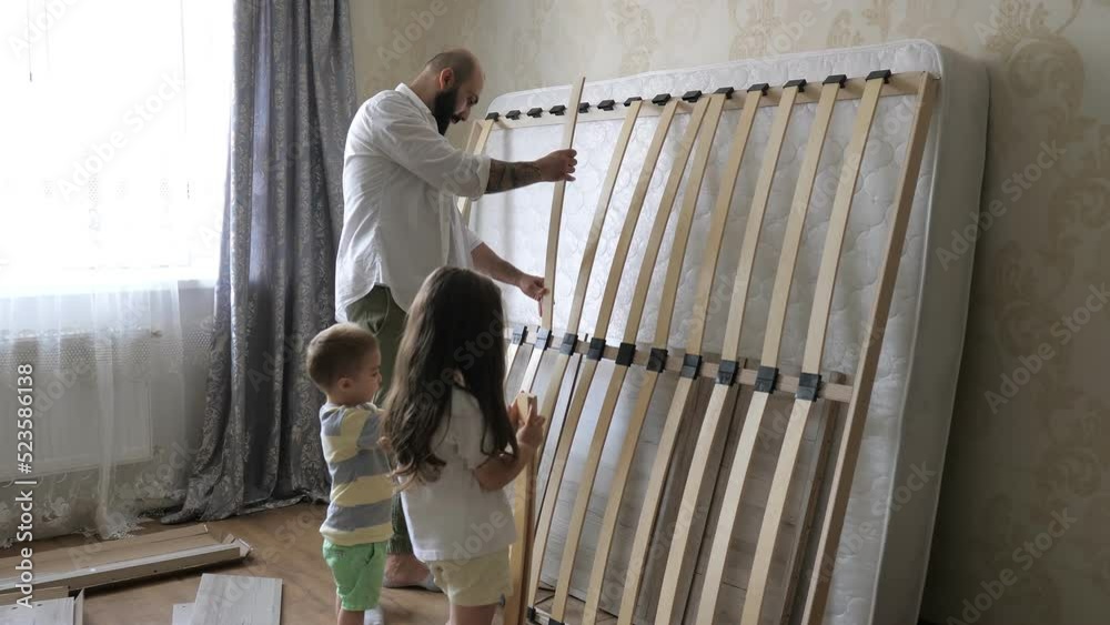 Dad with kids assembling wooden slats of an orthopedic base of a double ...