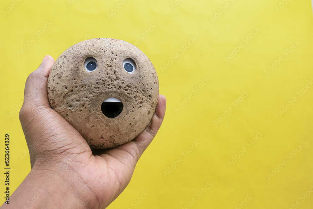 Man's hand holding a coconut shell emoji emoticon head on yellow paper ...