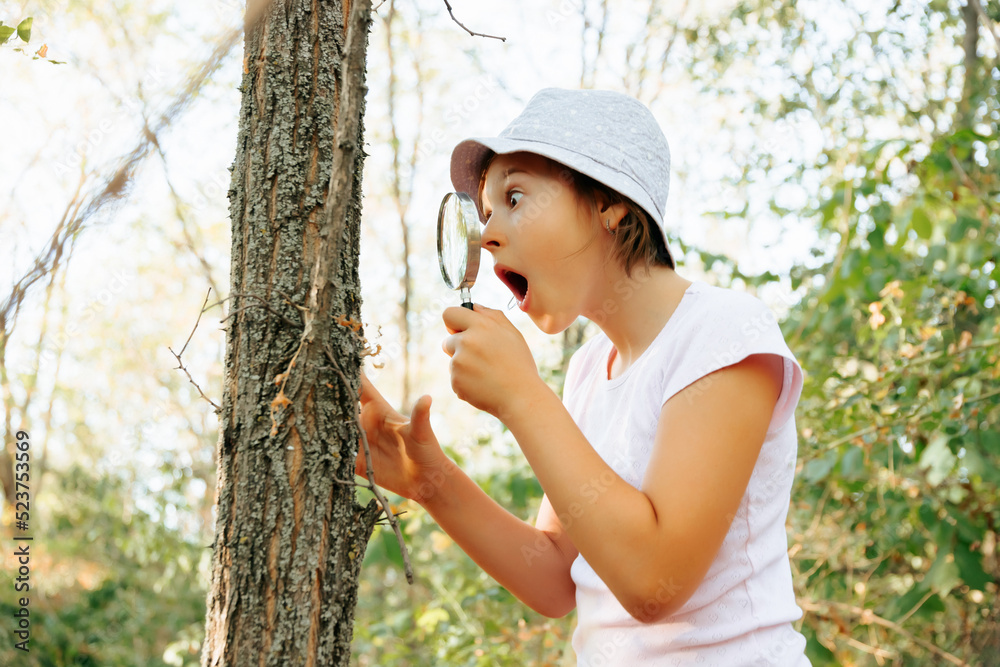 little child naturalist botanist with a magnifying glass is surprised ...