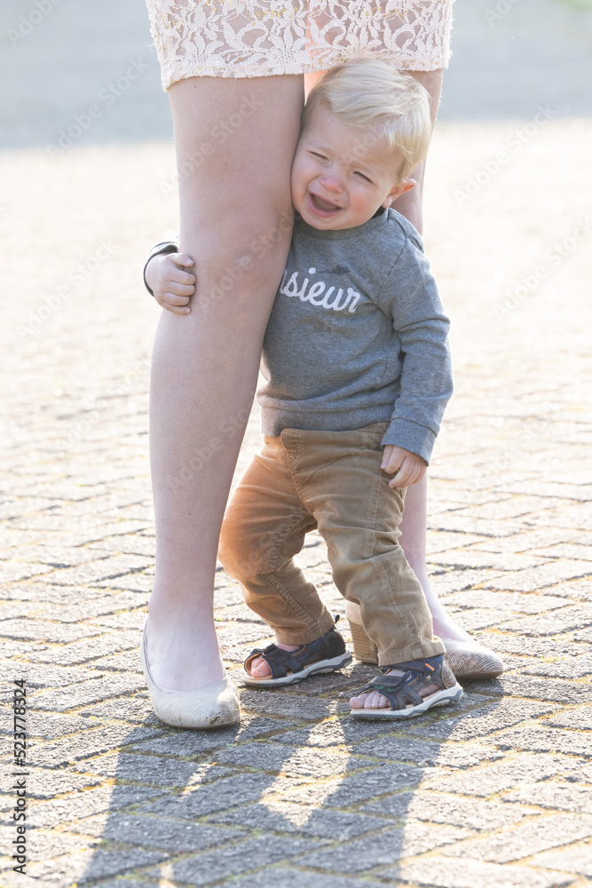 Sad caucasian blonde little boy hugging her mother legs. High quality ...