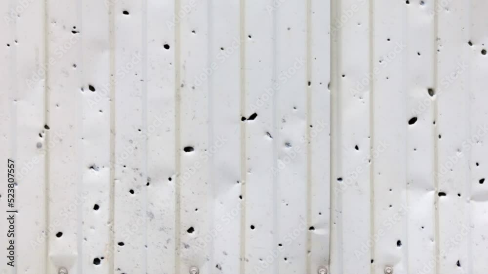 Close-up of a metal fence with bullet holes in the sunlight outdoors ...