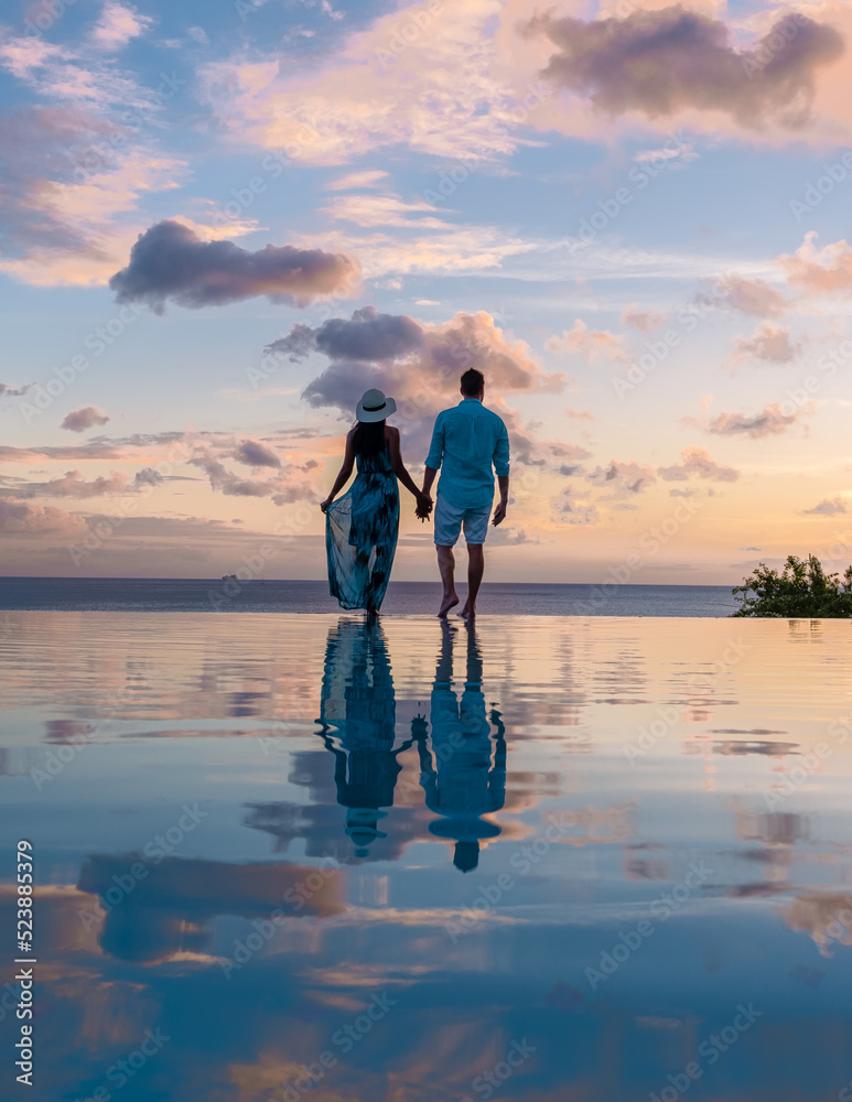 Young men and women watching the sunset with reflection in the infinity ...