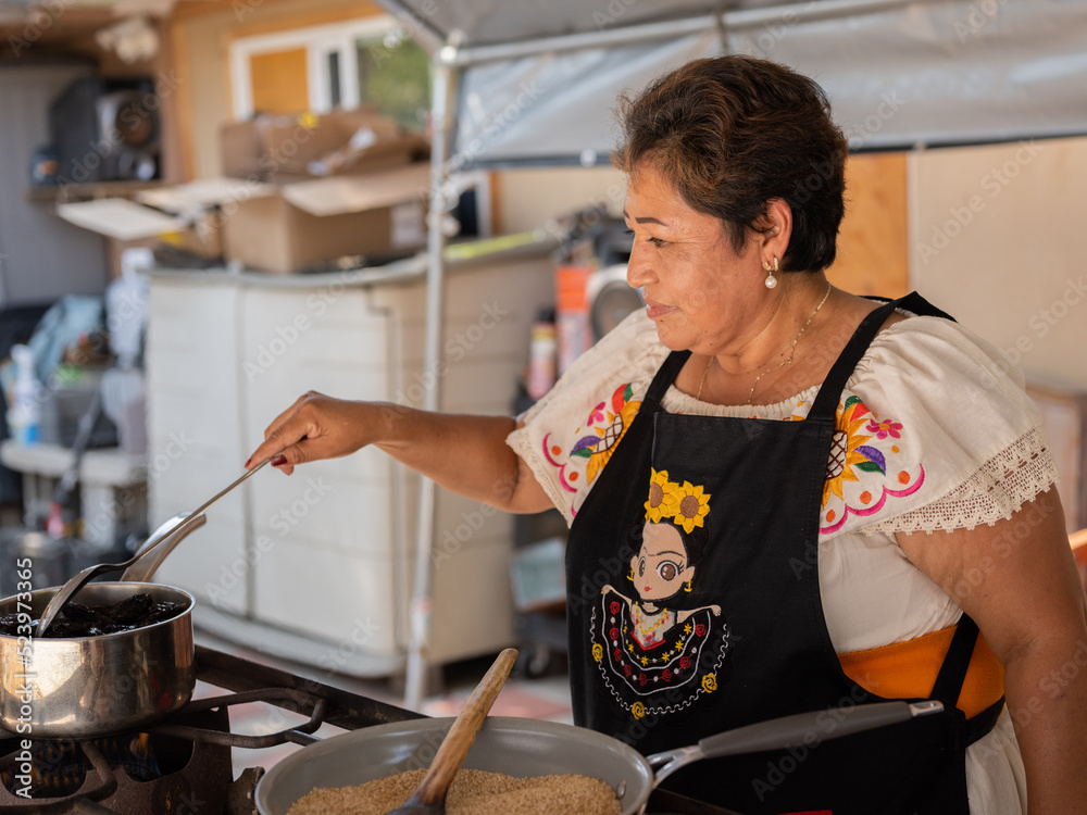 Horizontal image of an Indigenous woman cooking on a fry pan in an ...