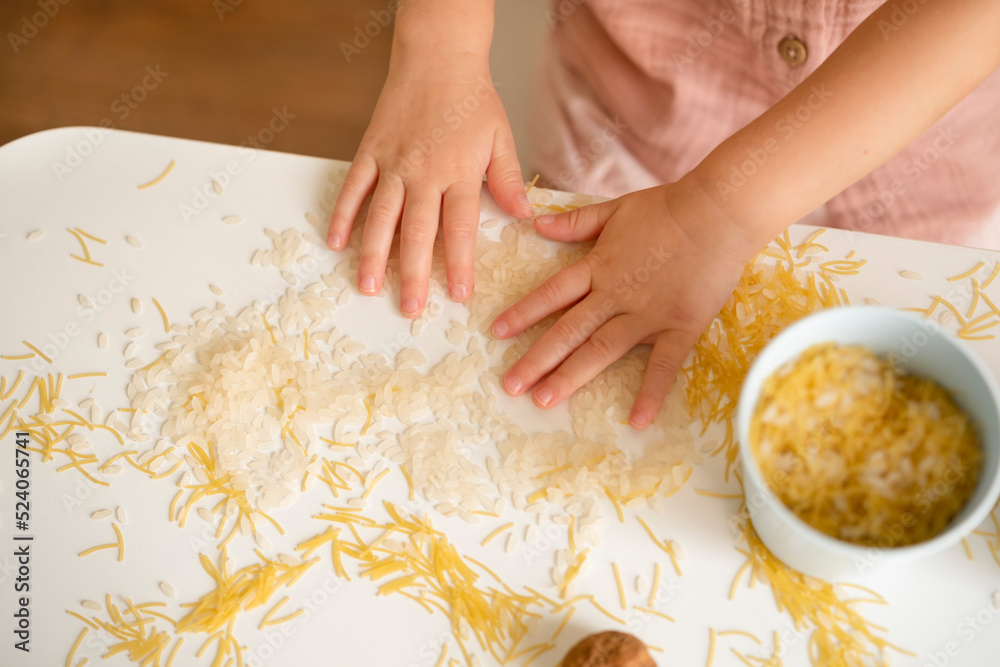 Baby hands playing with grain, nuts, pasta and rice at table.Sensorial ...