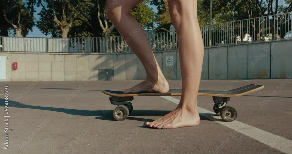 Handheld close-up side view of barefoot woman feet on skateboard slowly ...
