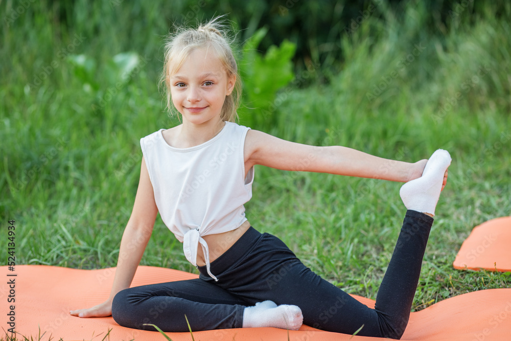 Child does outdoor sports exercises using fitness mat. Cute little girl ...