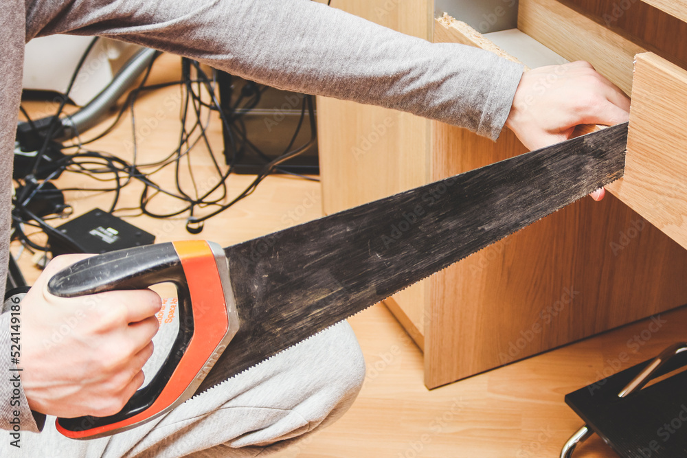 The hand of a young caucasian guy is sawing a board with a saw from the ...