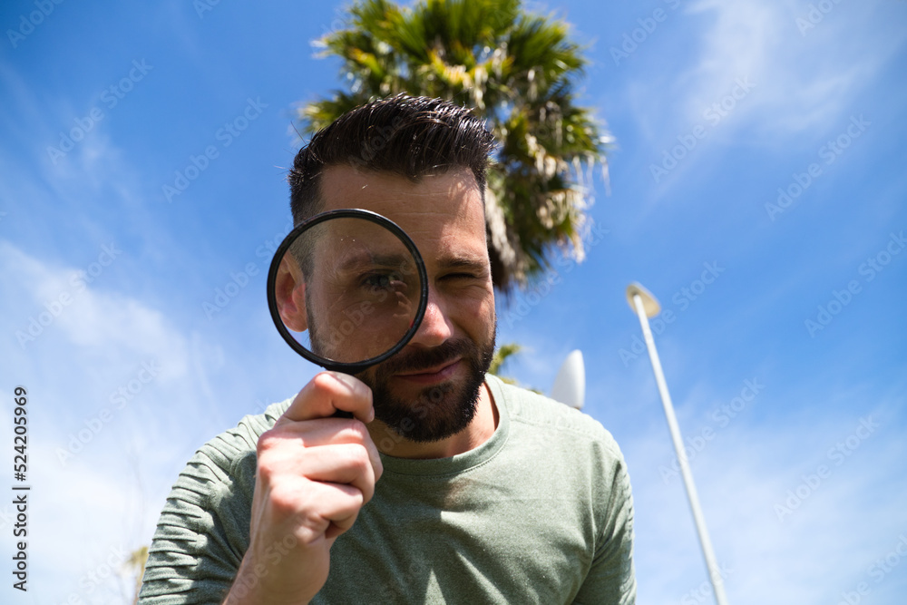 Handsome young man looks through a magnifying glass. His magnified eye ...
