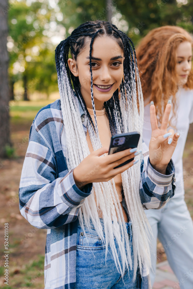 Young girl with afro pigtails holding phone showing v sign while ...
