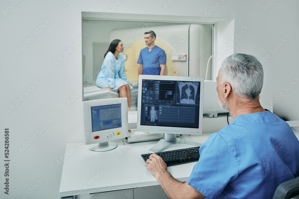 Doctor radiographer waiting in control room behind protective glass ...