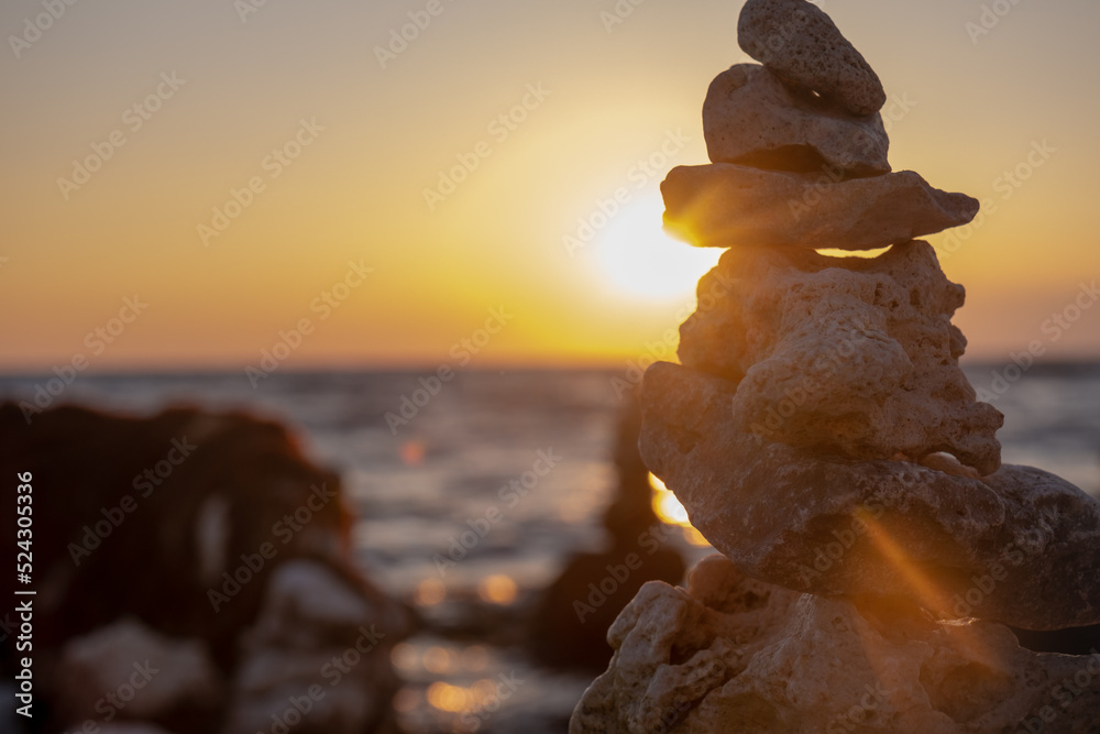 Stones stacked in a turret in the rays of the setting sun. Marine ...