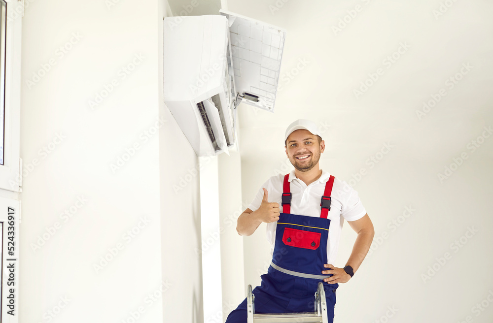 Happy young man in uniform standing on ladder under new air conditioner ...