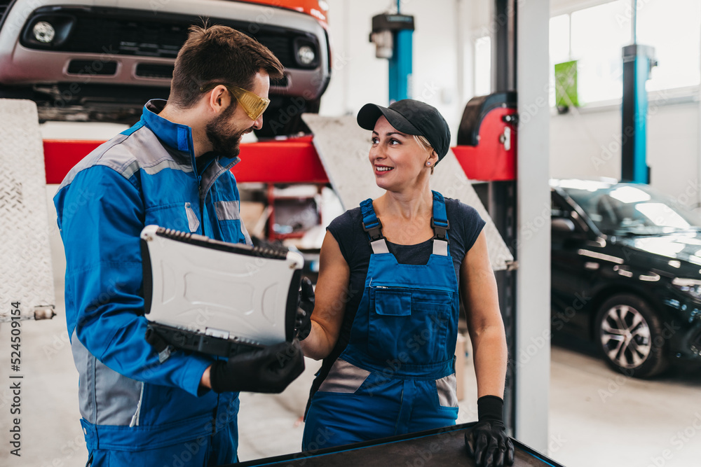 Male and female mechanics working together in large modern car repair ...
