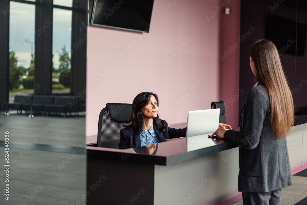 Young woman in formal suit talking with mature aged female receptionist ...