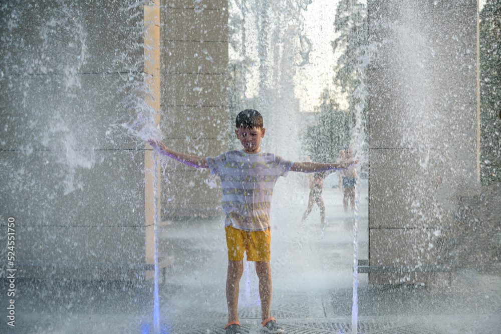 Boy having fun in water fountains. Child playing with a city fountain ...