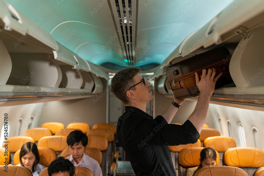 Caucasian businessman passenger finding seat in airplane and keep ...