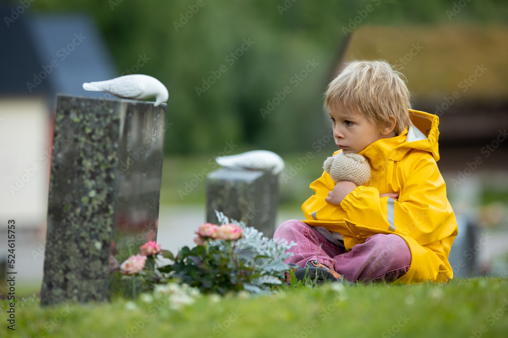 Sad little child, blond boy, standing in rain on cemetery, sad person ...