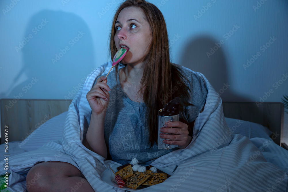 Woman late-night snacking in bed at home waking up hungry at night. Nighttime eating. Lady with ...