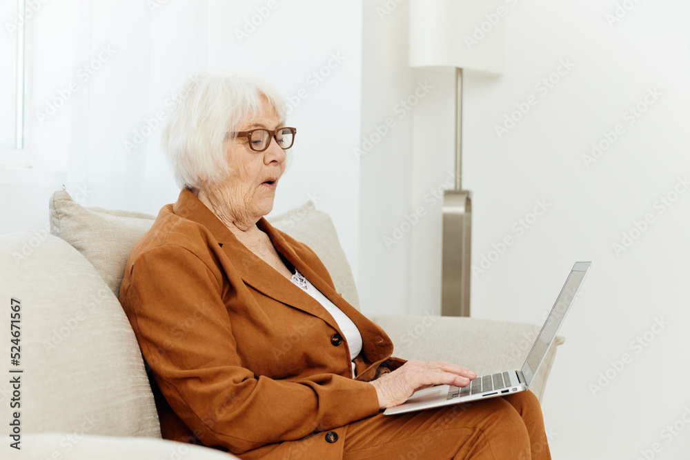 an elderly woman in suit is sitting on spacious sofa in a bright room ...