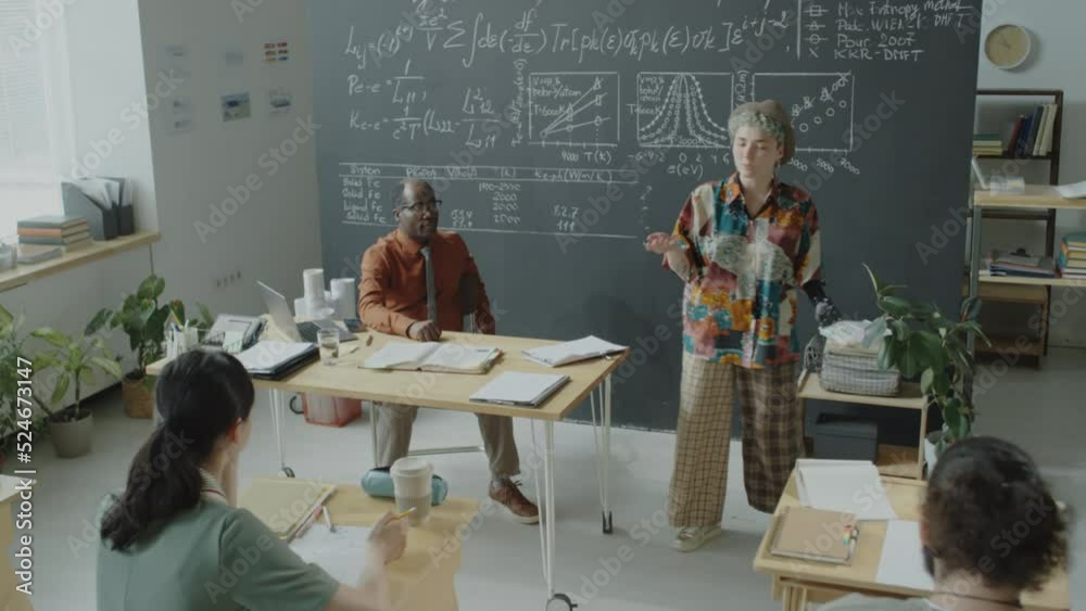 Tilt down shot of female student with prosthetic arm pointing at graphs ...