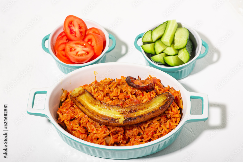 Jollof rice with fried banana. Fresh vegetables - tomato and cucumber ...