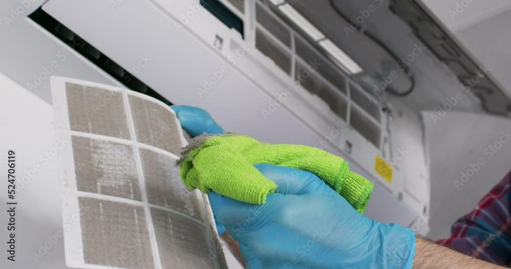 A man in gloves cleans the air conditioner filter with a green rag from ...