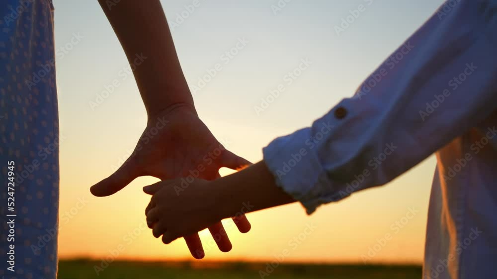 Close up of brother and sister holding hands against sunset in field ...