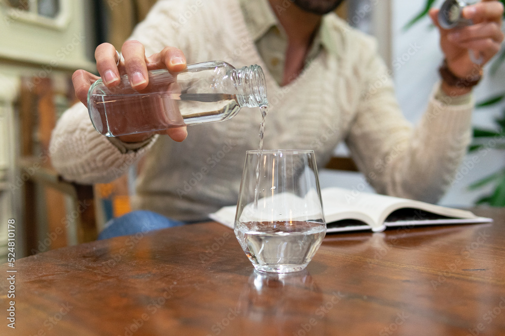 Faceless guy pouring water into glass while reading novel at home Stock ...