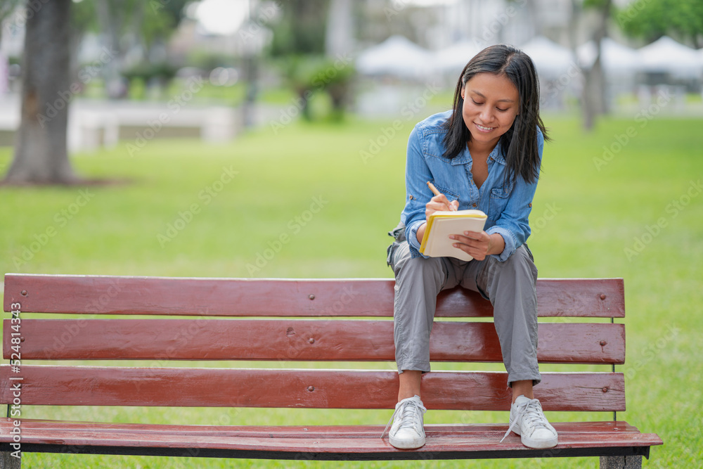 Ethnic woman sitting on bench and taking notes in notepad Stock Photo ...