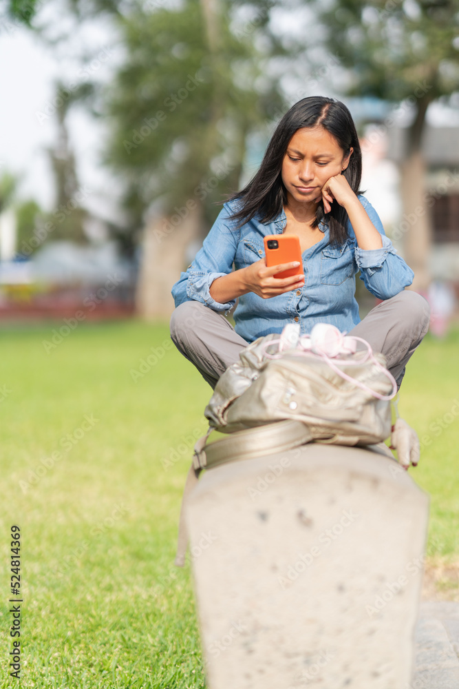 Bored ethnic woman scrolling smartphone in park Stock Photo | Adobe Stock