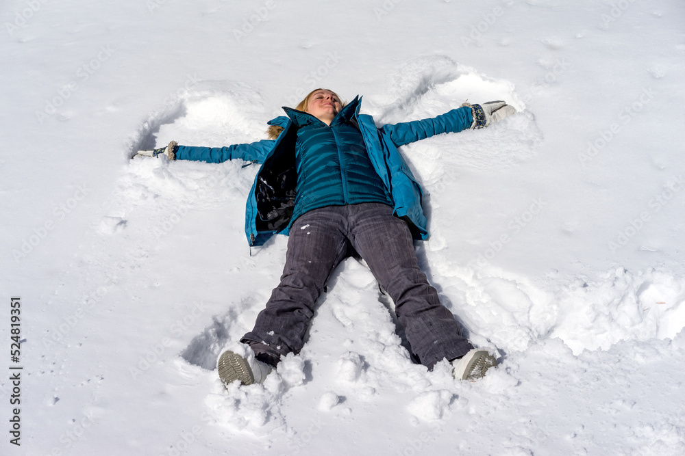 Beautiful young woman, lying down on a frozen snow, moving her arms and ...