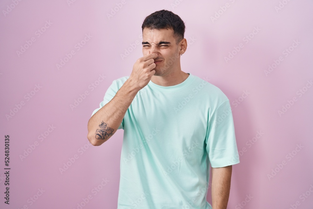 Handsome hispanic man standing over pink background smelling something ...