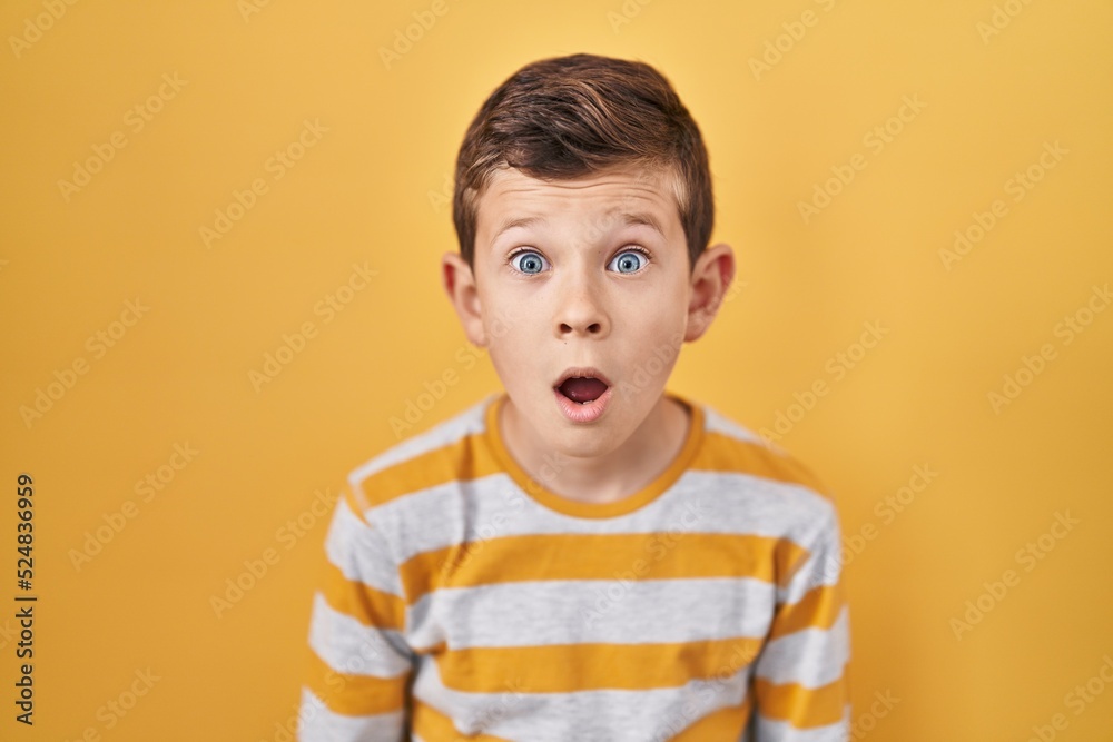 Young caucasian kid standing over yellow background afraid and shocked ...